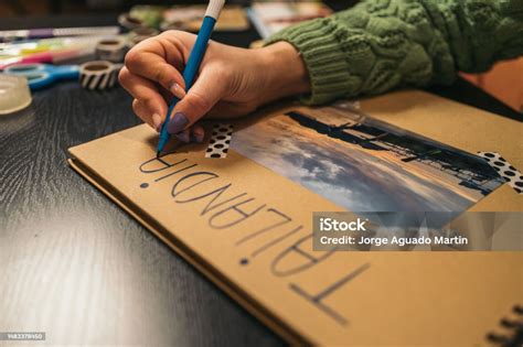 알아볼 수 없는 젊은 여성의 손은 여행 사진과 와시 테이프가 있는 수제 크래프트 앨범의 표지에 스페인어로 태국이라는 단어를 마커