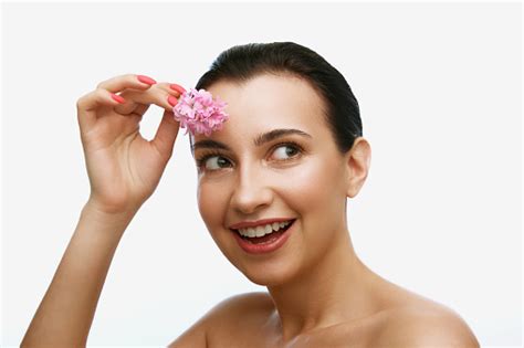 하얀 스튜디오 배경 위에 머리에 꽃을 들고 포즈를 취하는 벌거벗은 어깨를 가진 젊고 사랑스러운 여성의 초상화 스파 절차 25