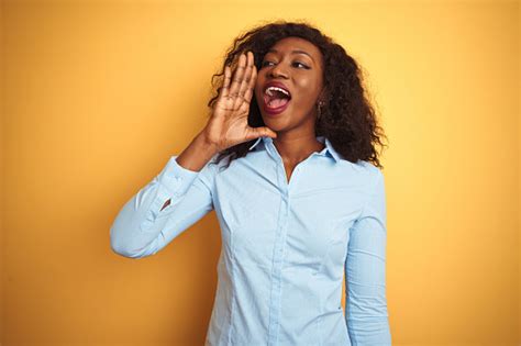 고립 된 노란색 배경 위에 우아한 셔츠를 입은 아프리카 계 미국인 사업가가 입에 손을 대고 큰 소리로 외치고 비명을 지르고 있습니다 통신 개념입니다 감정에 대한 스톡 사진