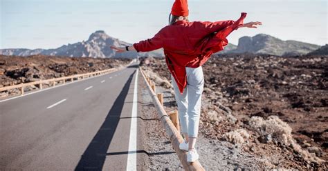 화창한 날에 화산 계곡 한가운데에 있는 도로 울타리를 걷고 있는 빨간 옷을 세련되게 입은 젊은 여성의 라이프스타일 초상화 평온한 라이프 스타일과 여행 컨셉 사진