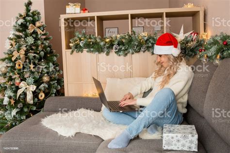 온라인 크리스마스 인사말 하얀 스웨터와 빨간 산타 모자를 쓴 여성은 노트북을 사용하여 친구 부모 및 온라인 쇼핑을 위해 화상 통화를합니다 12월에 대한 스톡 사진 및 기타