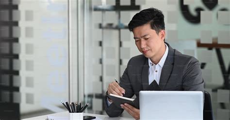 검은 양복을 입은 사업가가 노트북 컴퓨터로 작업하고 사무실 책상에 앉아 노트북에 메모를 하고 있다 사진 Unsplash의 앉아 이미지