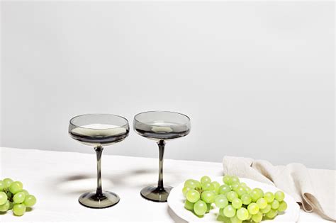 회색 샴페인 잔과 포도 옴 화이트 나무 테이블 트렌드 와인 유리 색상 넓은 샴페인 잔에 스파클링 화이트 와인이 있는 최소한의 여름 정물 측면도 복사 공간 가정 생활에 대한