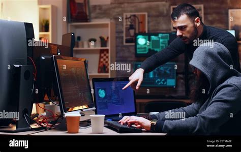 Dangerous Hooded Hacker And Her Partner Hacking The Government Planting A Malware Stock Photo