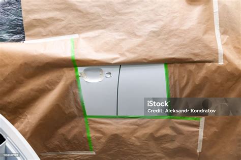 자동차 차체 수리를 위한 카메라의 사고 후 자동차 범퍼 및 도어의 부품은 부분적으로 종이로 덮여 있으며 흰색 색상으로 페인팅을 위한 녹색 마스킹 테이프로 붙여 넣어집니다