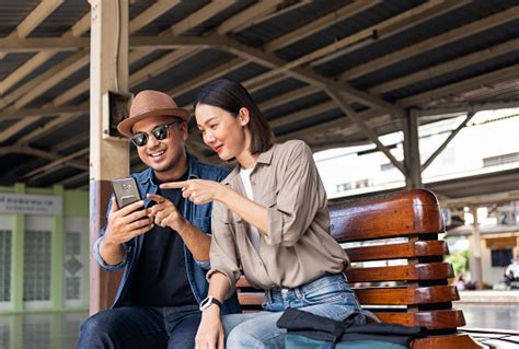 행복한 아시아 잘 생긴 남자와 선글라스 모자 및 배낭을 착용 한 아름다운 여자 배낭 여행자 그들은 기차역에서 휴대 전화로