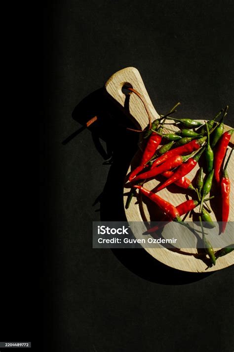 분위기 있는 조명이 있는 소박한 나무 도마에 올려진 빨간색과 초록색 칠리 페퍼 어두운 배경에 짙은 그림자를 드리우는 스파이시 태국 재료 질감과 색상 대비를 강조하는 미니멀한