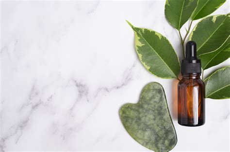 브랜드가없는 혈청 병 대리석 배경에 잎이있는 구아샤 얼굴 마사지 치료를위한 비취 얼굴 마사지기 안티 에이지 리프팅 및 토닝 처리 개념에 대한 스톡 사진 및 기타 이미지