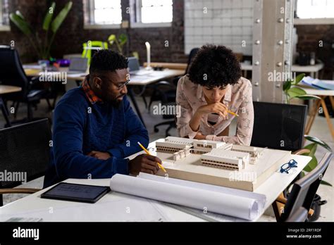 Diverse Male And Female Architects Looking At Building Model And Discussing Project At Office
