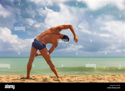 Rear View Of Muscular Male Swimmer On Beach Bending Over Sideways Stock