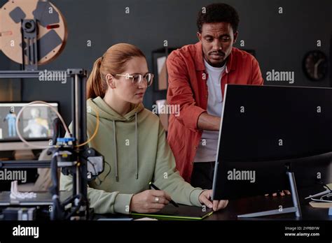 Two Colleagues Collaborating On Project In Modern Workspace Involving 3d Printing And Computer