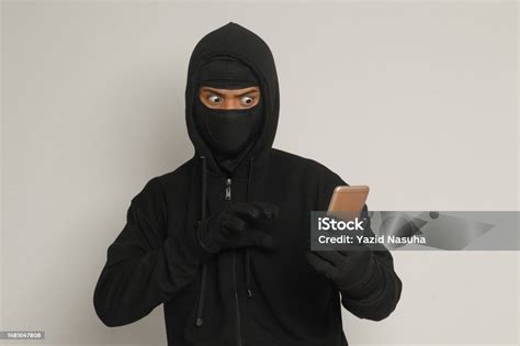 검은 후드티를 입고 휴대폰으로 해킹 활동을 하는 마스크를 쓴 수수께끼의 남자 스마트폰을 들고 있는 해커의 초상화 회색 배경에 격리된 이미지 20 24세에 대한 스톡 사진 및