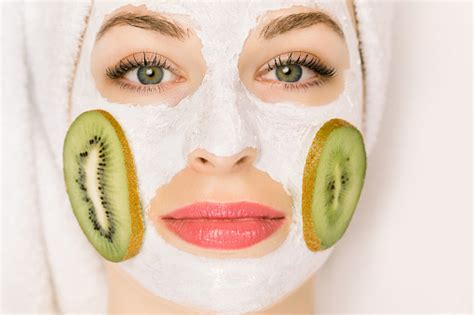 스파 절차 및 화장품 그녀의 얼굴 여자와 뺨에 키위 조각에 과일 마스크와 젊은 매력적인 여자의 얼굴의 상단 보기를 닫습니다 스파 살롱에서 머리에 목욕 수건과 건강관리와