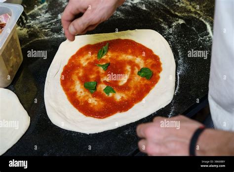 A Chefs Hand Carefully Places Fresh Basil Leaves On A Pizza Dough