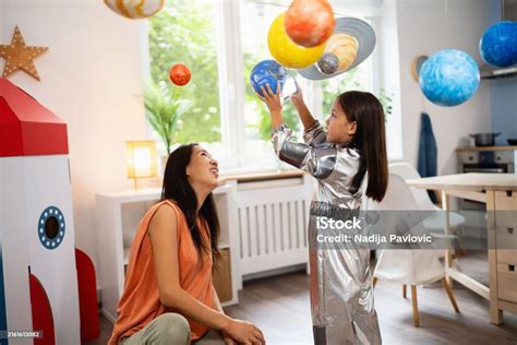Girl In A Space Suit Playing With Her Mom At Home Imagining Space