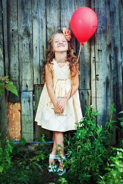 عکس با کیفیت دختر زیبا ایستاده در کنار دیوار چوبی با یک بادکنک قرمز در دست عکس با کیفیت و