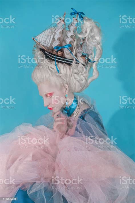 파란색 배경에 금발 머리를 가진 르네상스 공주 뷰티 메이크업 스튜디오에서 헤어 스타일로 배를 타고 동화 속 로코코 퀸 파란색 드레스의 모델 역사적인 헤어 스타일을 가진 여성