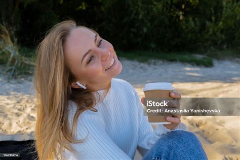 해변 바다 바다에서 종이컵 테이크아웃에서 커피를 마시는 행복한 젊은 여성 무선 헤드폰을 착용하고 오디오 치유 사운드 테라피를 마음챙김 자연 속의 여가 자연과의 웰빙 단결