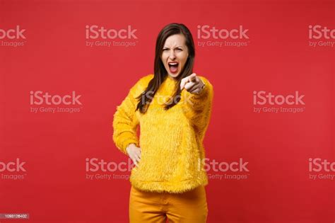 염증된 젊은 여자 카메라 노란색 모피 스웨터 포인팅 검지 손가락에 비명과 맹세에 고립 된 빨간 배경 스튜디오 사람들이 진심으 감정 라이프 스타일 개념 복사 공간을 비웃는 다