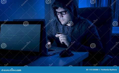 Portrait Of Male Hacker Holding Credit Card And Typing Fraud Program