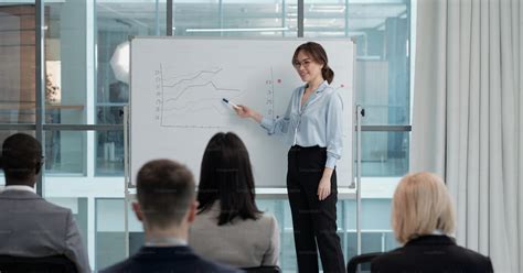 행복한 젊은 현대 여성 경제학자가 금융 변동을 발표하는 동안 화이트보드의 그래프를 가리키고 있다 사진 Unsplash의 사업 이미지