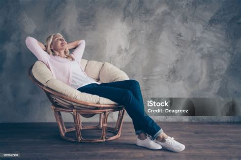 흰색 고리버들 안락 의자 꿈에 누워 평화로운 진정 중년 여성의 전체 길이 사진은 방에 파스텔 색상 스웨터 데님 청바지를 착용 가정 생활에 대한 스톡 사진 및 기타 이미지