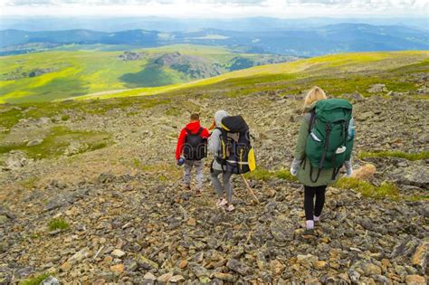 3 туриста 2 девушки и один мальчик с рюкзаками идут вниз с Стоковое Фото изображение