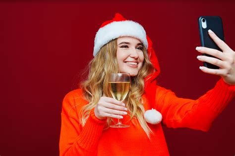 빨간 배경에 샴페인과 스마트폰이 있는 산타클로스 모자를 쓴 여자 12월에 대한 스톡 사진 및 기타 이미지 12월 가상 이벤트 개념 Istock