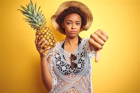 화가 얼굴 엄지 손가락으로 싫어하는 것을 보여주는 부정적인 기호 거부 개념과 노란색 고립 된 배경 위에 소나무를 들고 아프리카 계 미국인 여성 개념에 대한 스톡 사진 및