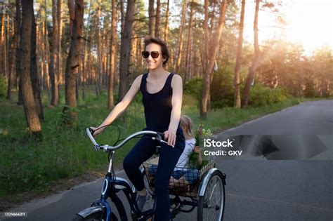 젊은 성인 백인 엄마는 밝은 화창한 날에 아름다운 시골 시골 길에서 야생 필드 꽃을 들고 귀여운 사랑스러운 금발 딸과 함께 자전거를 타는 여가 재미를 즐깁니다 시골 휴가