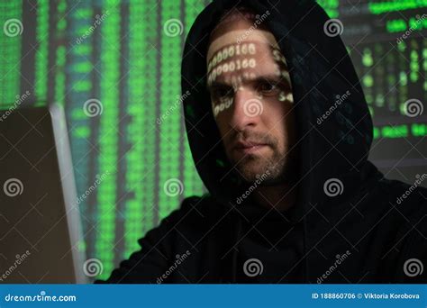 Male Hacker Working On A Computer While Green Code Characters Reflect On His Face In A Dark