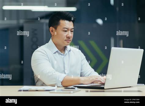 A Young Man Of Asian Origin Programmer Developer Works In The Office At A Desktop Using A