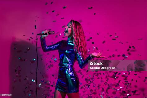 그녀가 스포트라이트를 껴안으면서 빛나는 색종이 조각과 함께 네온 조명이 켜진 분홍색 배경에서 열정적으로 노래하는 매력적인 젊은 여성 16 17 살에 대한 스톡 사진 및 기타
