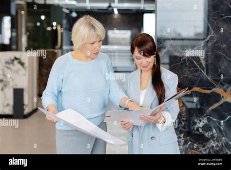 Two Women Engaged In A Collaborative Discussion In A Modern Office Reviewing Documents And