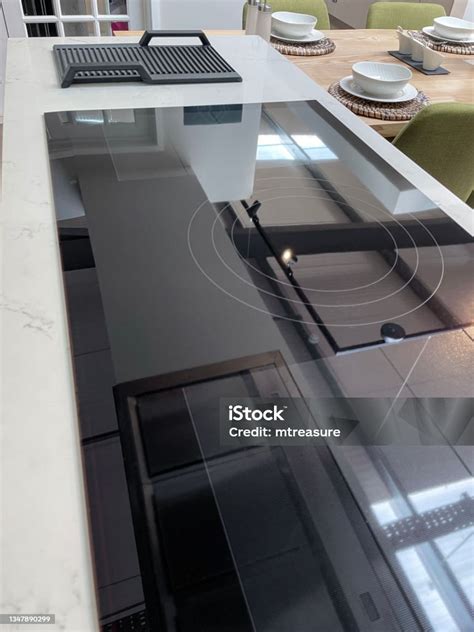 흰색 접시와 그릇 둥근 고리버들 플레이스 매트 검은 세라믹 호브 밥솥 철판 팬이있는 주방 카운터 옆에있는 식사를위한 나무 주방 식탁 세트 의 이미지 번철에 대한 스톡 사진