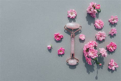 홈 스파를위한 얼굴 마사지 도구 장미 새싹이있는 회색 파스텔 배경에 장미 석영으로 만든 얼굴 롤러 자연 치료 개념 상단 보기