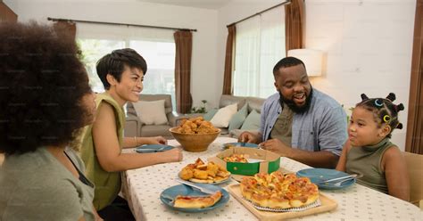 행복한 아프리카 가족 부모와 두 어린 딸이 함께 프라이드 치킨과 피자를 먹고 있습니다 아버지와 어머니와 귀여운 아이 소녀 아이가 집에서 함께 먹고 즐겁게 식사를 나누고