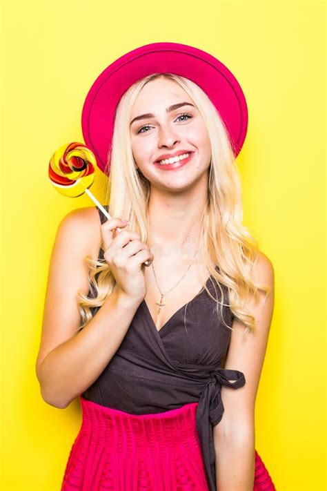 Довольно белокурая сексуальная красивая женщина с леденцом на палочке на желтой предпосылке
