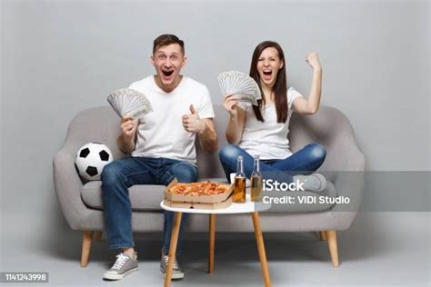 행복 한 커플 여자 남자 축구 팬 지원 선호 하는 팀 돈의 팬을 들고 달러 지폐 현금 돈에서 우승 제스처 회색 배경에 고립 스포츠 가족 레저 라이프 스타일 개념입니다 가족에