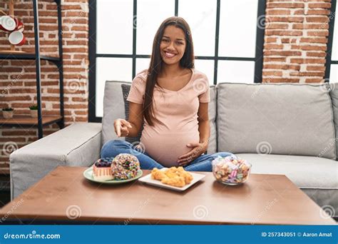 Young Pregnant Woman Eating Sweets At Home Smiling Happy Pointing With