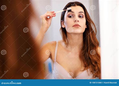 Giovane Donna Attraente Che Fa Trucco Mentre Esaminando Lo Specchio In Bagno Fotografia Stock