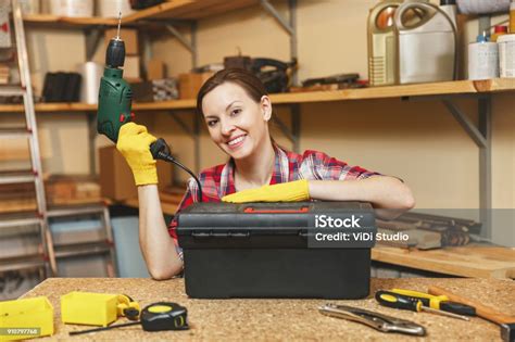 아름 다운 웃는 백인 젊은 갈색 머리 여자 격자 무늬 셔츠 회색 T셔츠 노란색 장갑 나무 테이블 장소에 목공 워크숍에서 작업 도구 상자 다른 도구에서 전원 훈련 했다 Diy