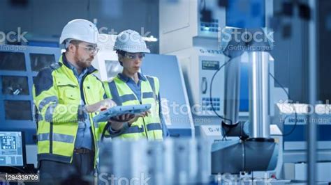 공장 워크샵 전문 여성 엔지니어 남성 기계 작업자는 산업 용 디지털 태블릿 컴퓨터를 사용하여 작업하고 생산 라인을 위한 로봇