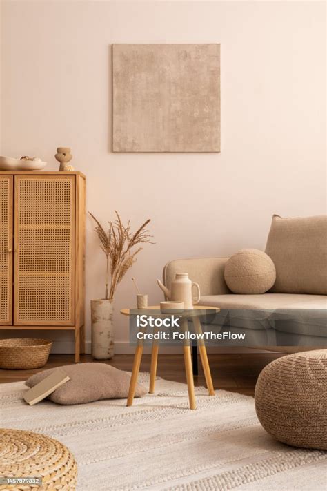 베이지색 소파 둥근 나무 커피 테이블 갈색 푸프 등나무 화장실 말뚝 및 개인 액세서리가 있는 햇살이 잘 드는 밝은 인테리어 가정