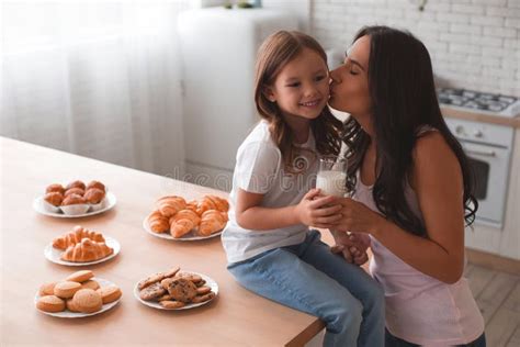 Madre Besando A Su Hija Sentada En La Mesa De La Cocina Imagen De