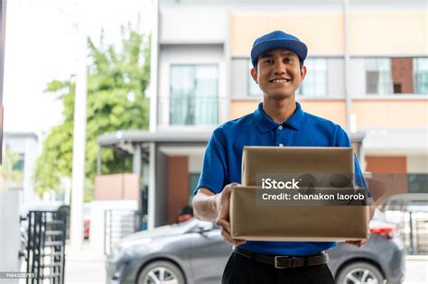 파란 제복의 손에 소포를 가진 아시아 납품 남자는 좋은 서비스로 온라인 쇼핑에서 집 앞의 고객 앞에 소포를 보냅니다 택배 남자는 목적지에 포장을 보냅니다 고객에 대한 스톡