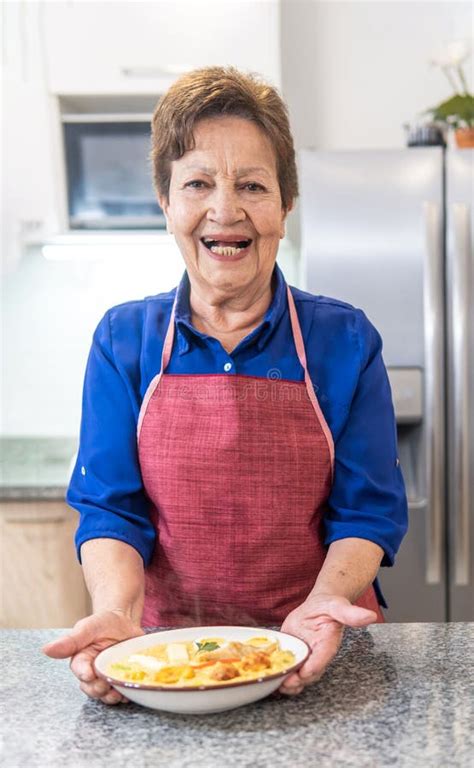 Smiling Older Adult Woman Offering A Plate Of Fanesca Looking At The