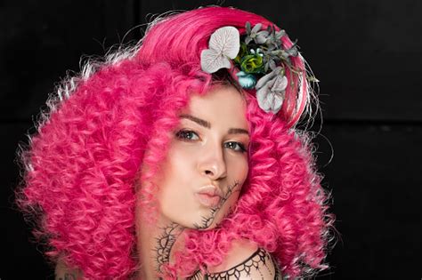 아프리카 스타일 곱슬 밝은 분홍색 머리와 젊은 매력적인 백인 여자 모델의 초상화 문신 얼굴과 꽃 그녀의 머리에 짠 검은 배경에 스튜디오에서 사진 감정에 대한 스톡 사진 및