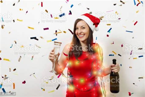 아름 다운 백인 웃는 젊은 행복 한 여자 빨간 드레스 크리스마스 모자와 손전등 유리와 흰색 바탕에 샴페인의 병을 화 환에 산타 소녀 격리입니다 새 해 휴일 2018년에 대한
