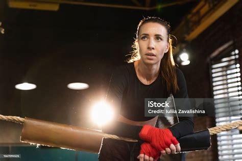 여자 파이터 걸 파워 빨간 권투를 한 여자 파이터는 권투 링에 서서 보호 붕대를 감고 밧줄에 기대어 휴식을 취합니다 강한 강력한